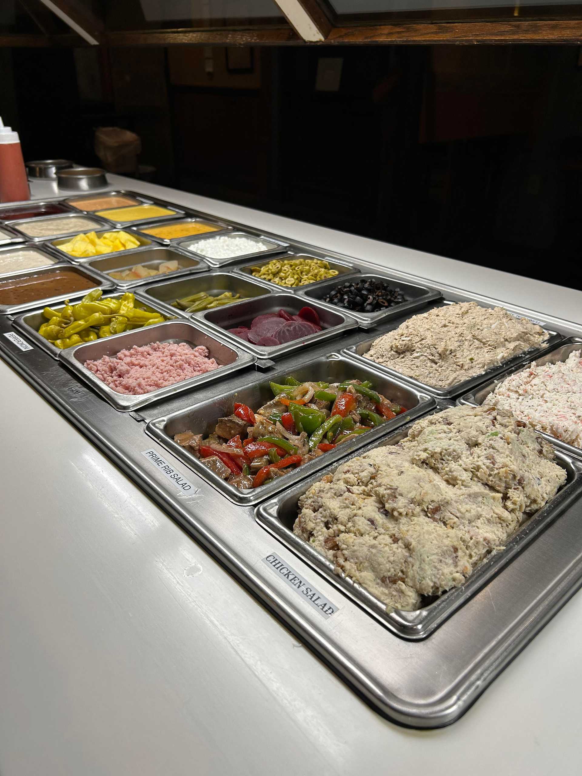 Self-serve salad bar with various fresh toppings in metal containers ...